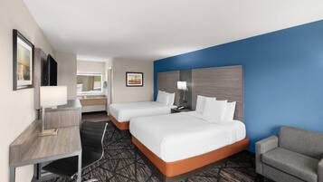 Quarto de hotel com duas camas, uma mesa, uma cadeira e uma televisão.