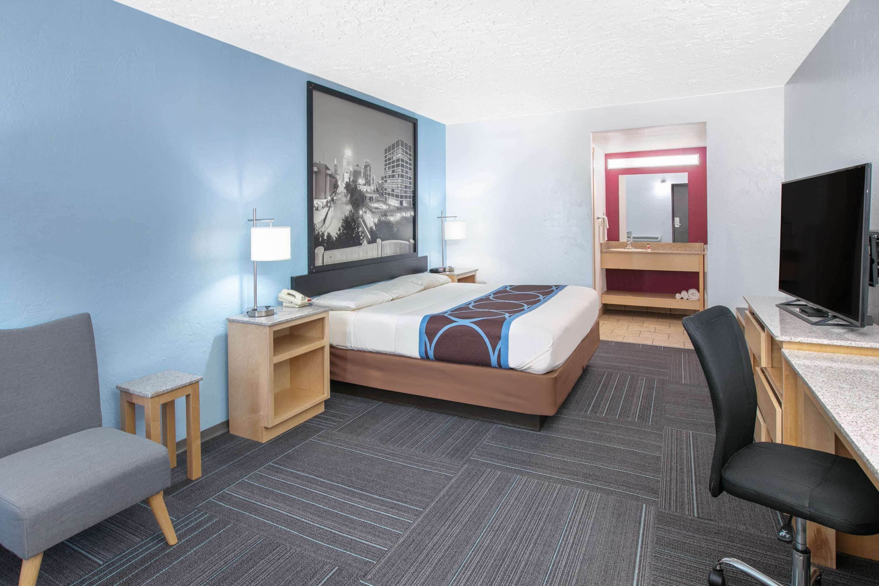 Quarto de hotel com cama, mesas de cabeceira, escrivaninha, cadeira, televisão e uma janela grande.