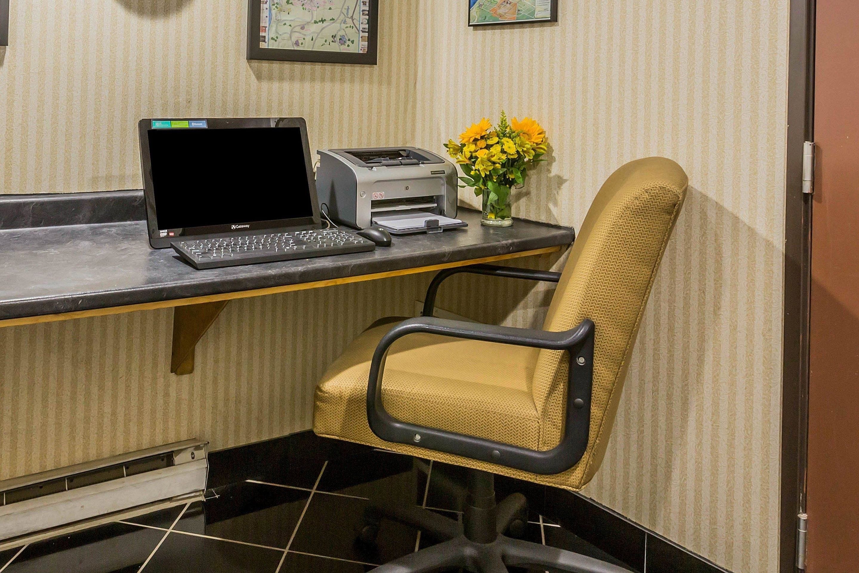 Uma mesa com um laptop, uma impressora e um vaso de flores.