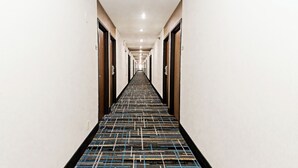 Um corredor de hotel comprido e estreito, com carpete estampado, portas em ambos os lados e teto com iluminação embutida.