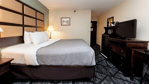 Quarto de hotel com cama, escrivaninha, televisão e abajur.