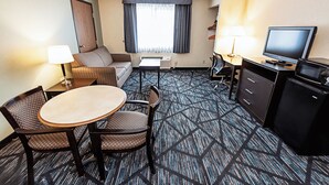 Quarto de hotel com sofá, uma pequena mesa, TV, escrivaninha e minibar.