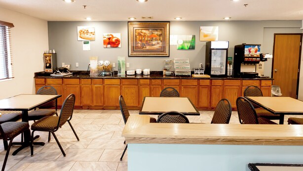 Uma sala de jantar de hotel com armários de madeira, uma máquina de café e quadros nas paredes.