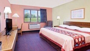 Quarto de hotel com cama, escrivaninha com televisão, cadeira, janela com vista e ar condicionado.
