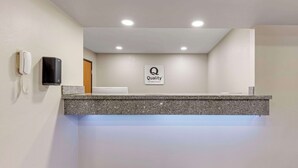 Uma área de recepção com balcão de granito, um letreiro com a palavra 'Quality', um telefone e uma porta.
