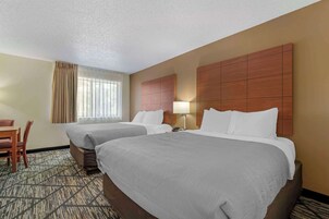 Quarto de hotel com duas camas, uma escrivaninha e uma cadeira.