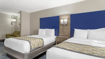 Quarto de hotel com duas camas, uma escrivaninha, uma cadeira e um abajur.