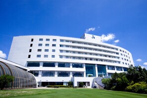 Um edifício moderno de vários andares com telhado plano, grandes janelas e um sinal 'JS' bem visível no topo.