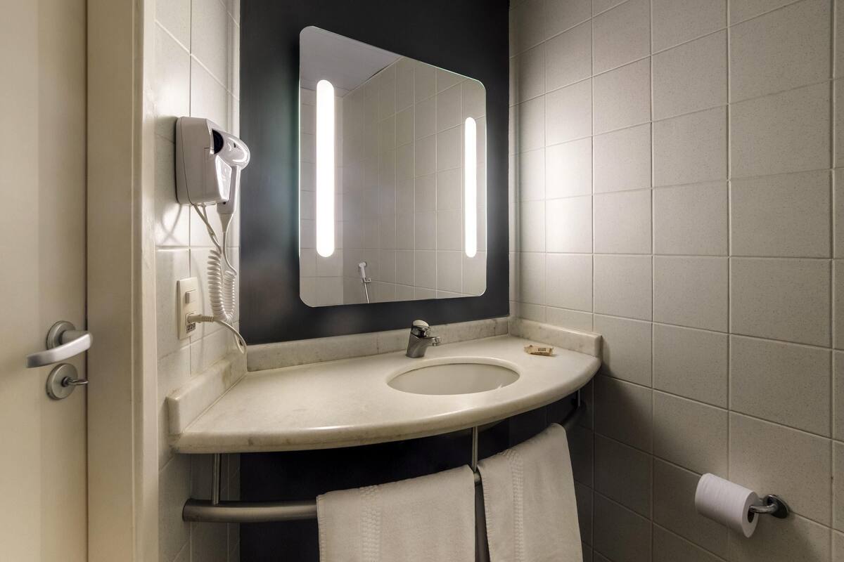 Um banheiro com pia, espelho, porta-toalhas e suporte para papel higiênico.