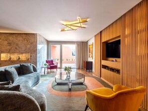 Uma sala de estar moderna com sofá, poltrona amarela, mesa de centro de vidro, TV de tela plana fixada em um painel de madeira e vista para a varanda externa.