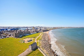Uma cidade costeira com calçadão, praia e edifícios industriais.