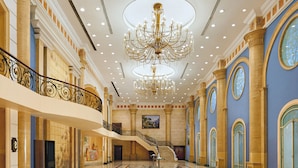 Um hall imponente com um lustre grande, pisos de mármore e uma escadaria que leva a um andar superior.