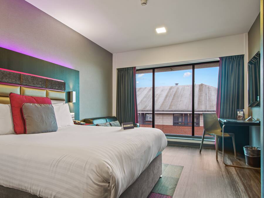 Quarto de hotel moderno com uma cama grande, uma escrivaninha e vista para a cidade.