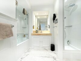 Uma casa de banho moderna com chuveiro em cabine de vidro, chão em mosaico de mármore e toucador com lavatório e espelho.
