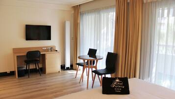 Quarto de hotel com cama, escrivaninha, cadeira, televisão e janela com cortinas.