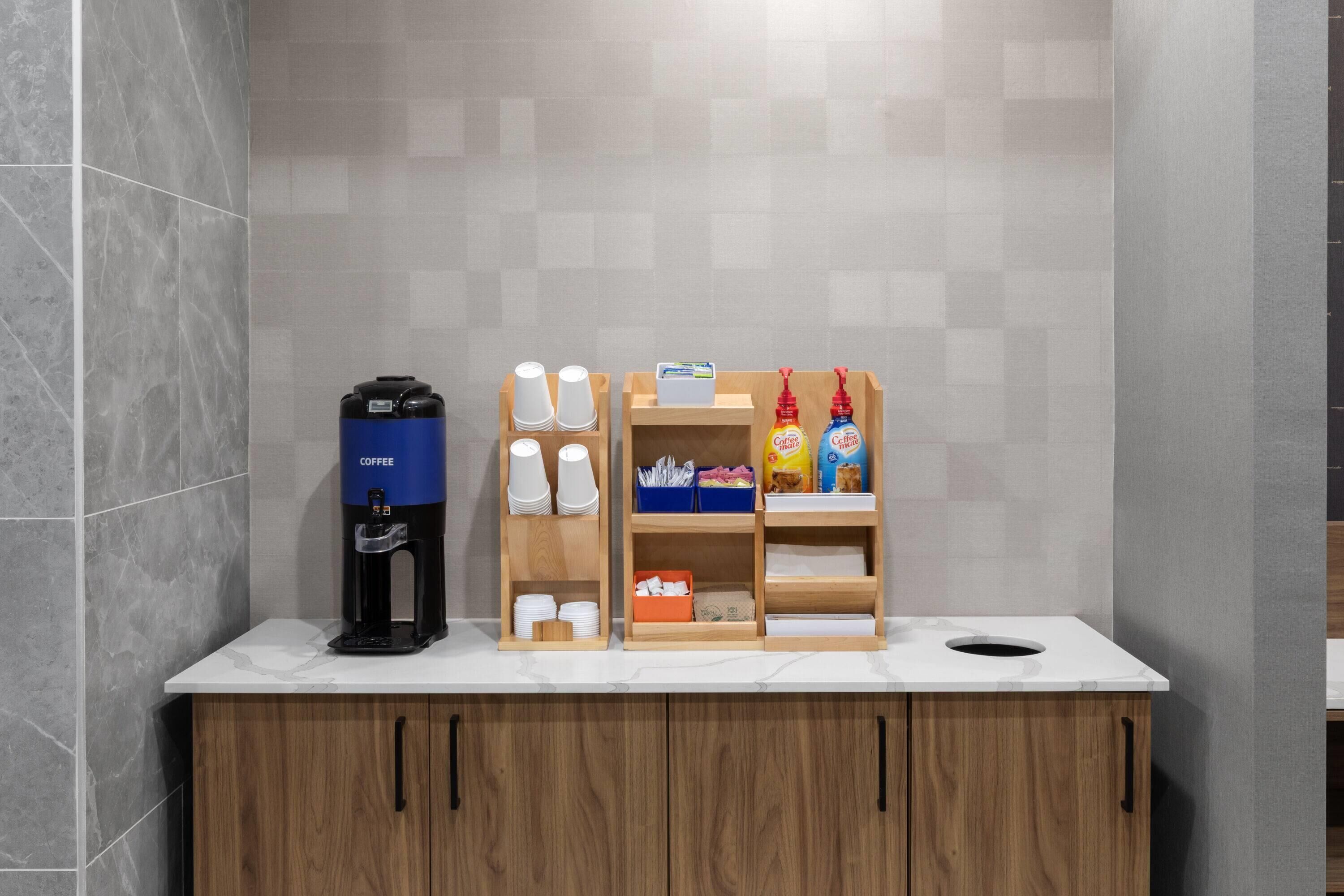 Um espaço com estação de café, dispensador, xícaras e acompanhamentos.
