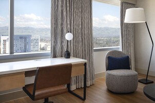 Um espaço de escritório moderno com escrivaninha, cadeira, luminária e vista para montanhas.