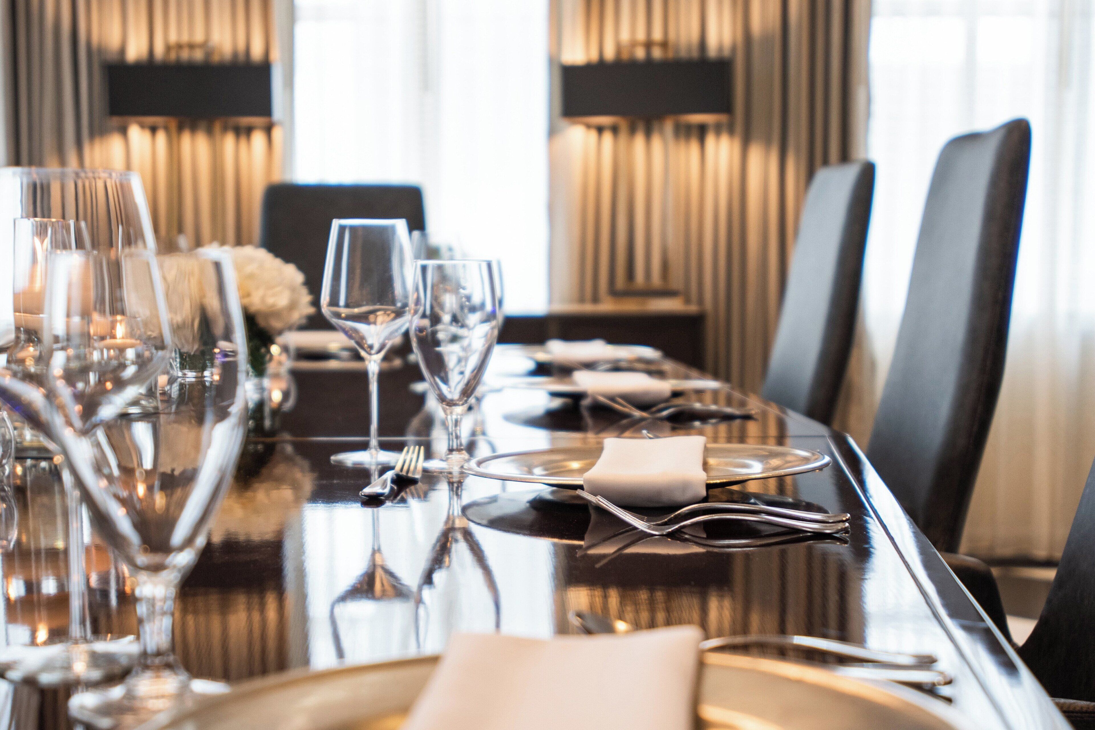 Uma mesa de jantar posta para uma refeição formal, com vários copos de vinho, pratos e talheres.