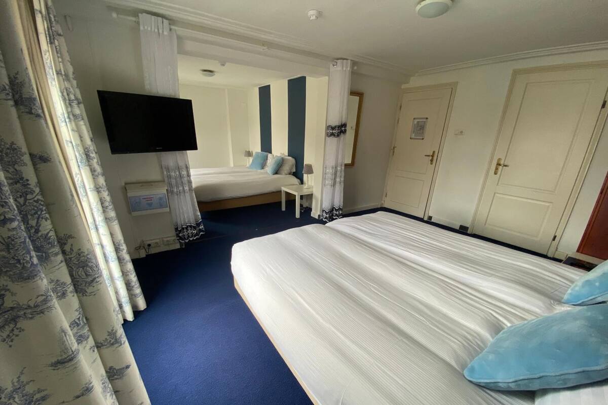 Quarto de hotel com uma cama grande, uma cama menor, uma TV e uma escrivaninha.