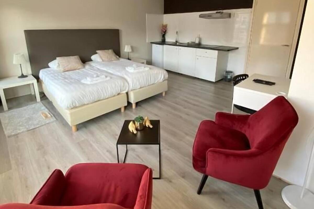 Quarto moderno com uma cama grande, uma cadeira vermelha e uma pequena mesa com uma planta.