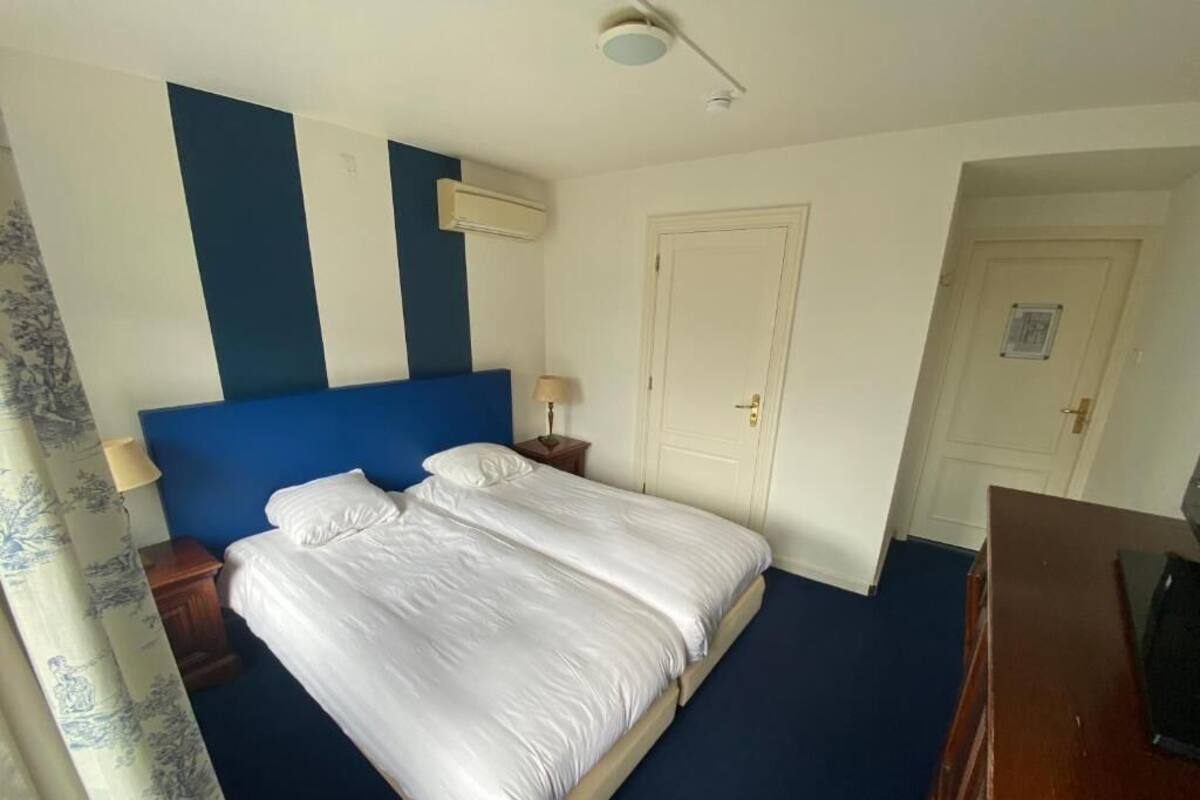 Quarto com uma cama grande, mesa de cabeceira, escrivaninha e porta.
