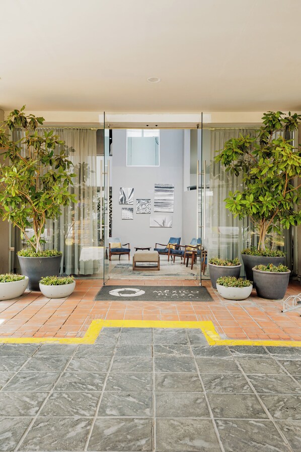 Um lobby moderno com portas de vidro, plantas em vasos e uma área de estar com cadeiras e um banco.