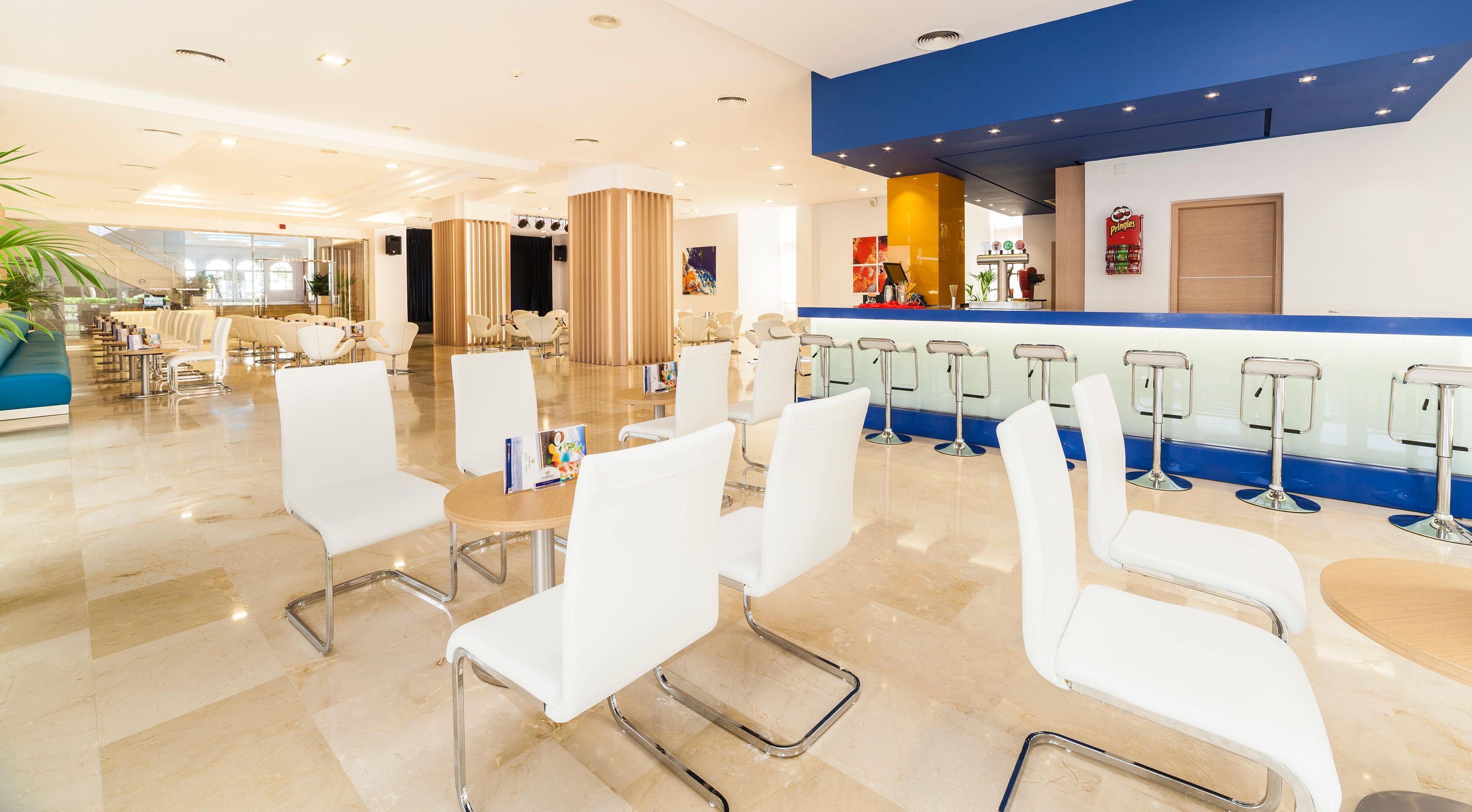 Um saguão de hotel com cadeiras brancas, um balcão de recepção e uma área de bar.