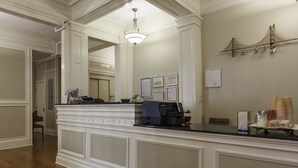 Uma área de recepção com balcão de mármore, lustre, quadros com certificados nas paredes e um espaço para café.