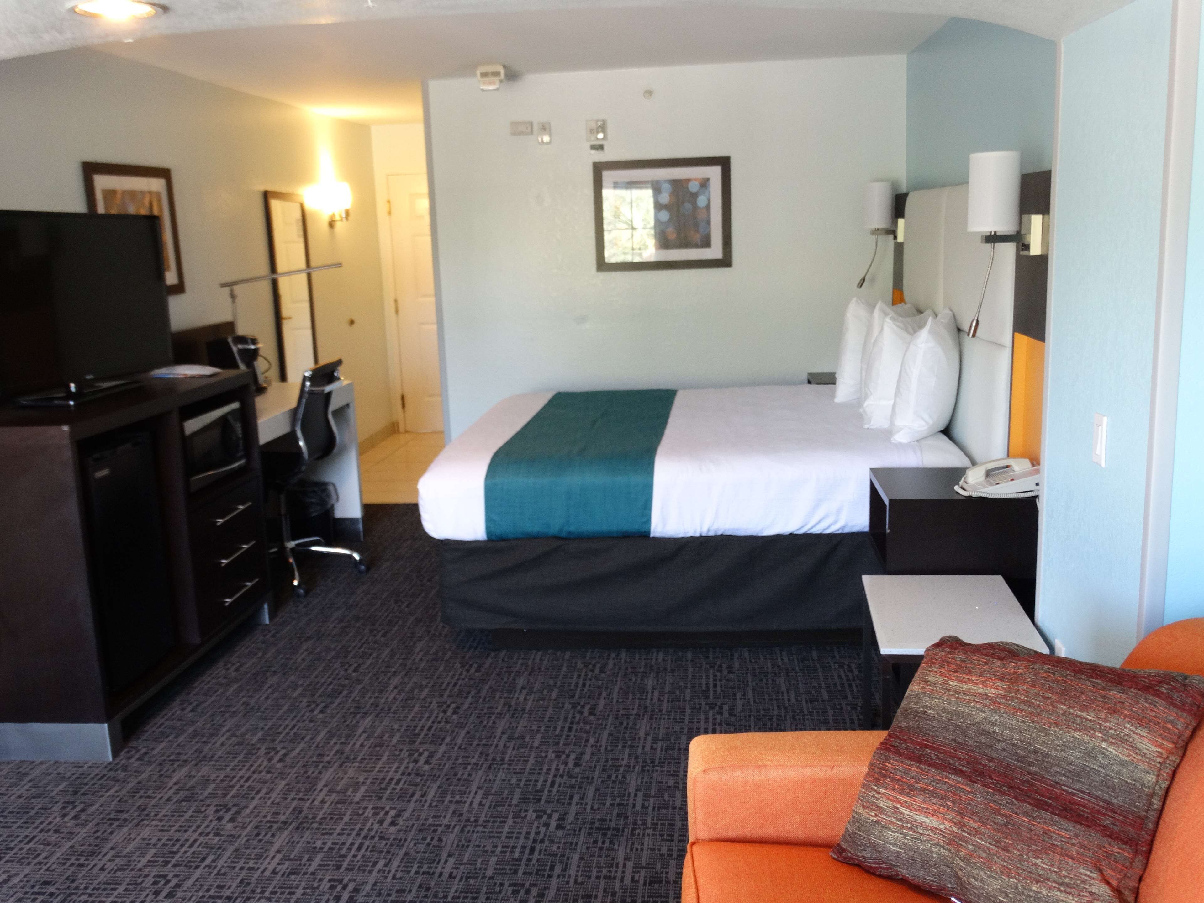 Quarto de hotel com cama, escrivaninha, televisão e sofá.