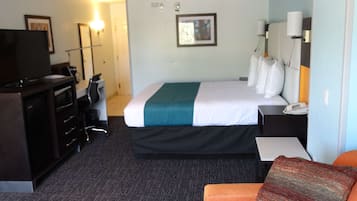 Quarto de hotel com cama, escrivaninha, televisão e sofá.