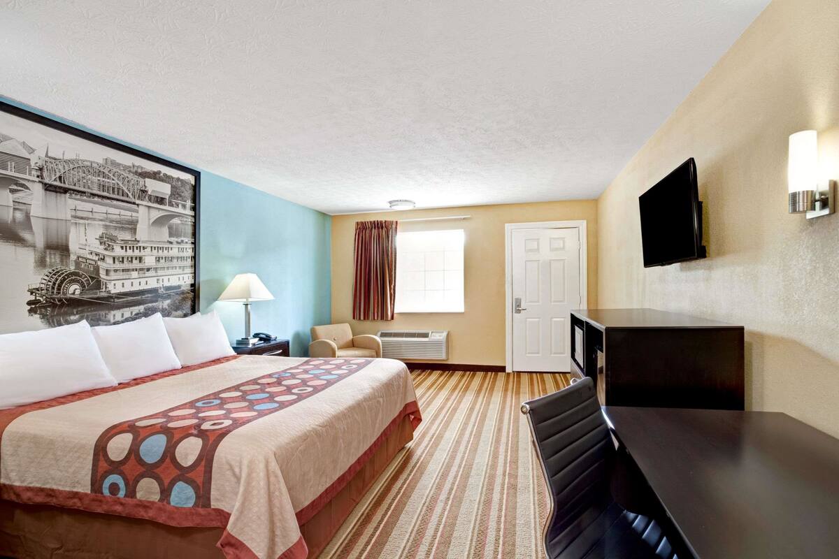 Quarto de hotel com uma cama grande, televisão de tela plana, escrivaninha, cadeira, janela com cortinas e televisão na parede.