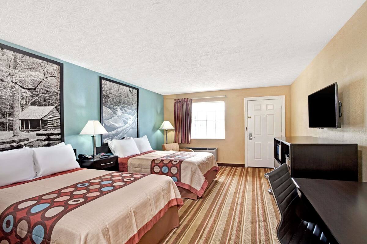 Quarto de hotel com duas camas, televisão, escrivaninha e janela com cortinas.