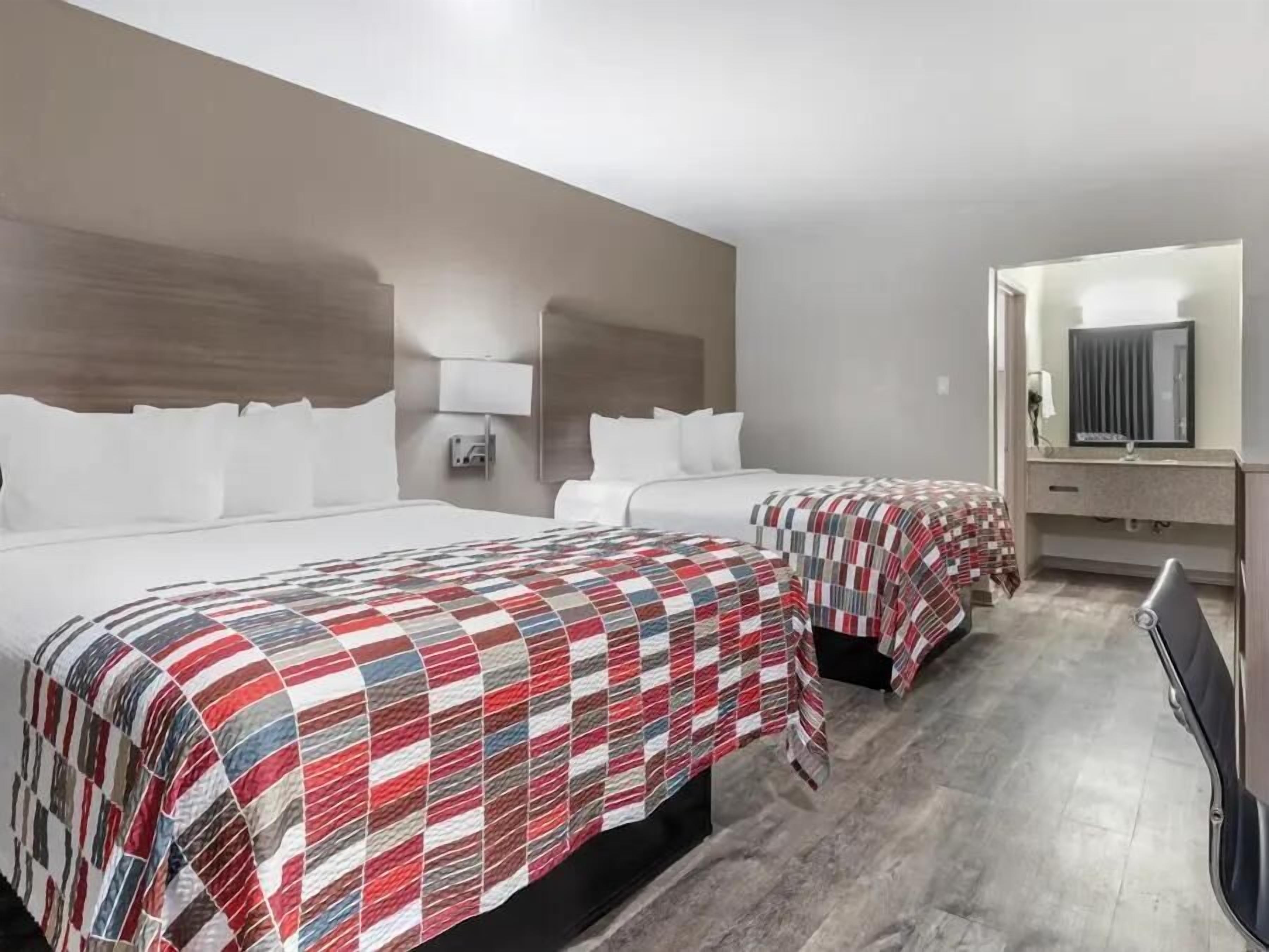 Quarto de hotel com duas camas, banheiro e espelho.
