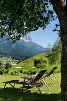 Uma área de estar tranquila ao ar livre, com cadeiras de apoio e uma mesa, com vista para um vale verdejante e montanhas distantes.