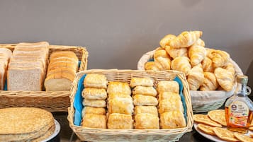 Diversos produtos de panificação, incluindo pão, croissants e doces, expostos em cestas e pratos.