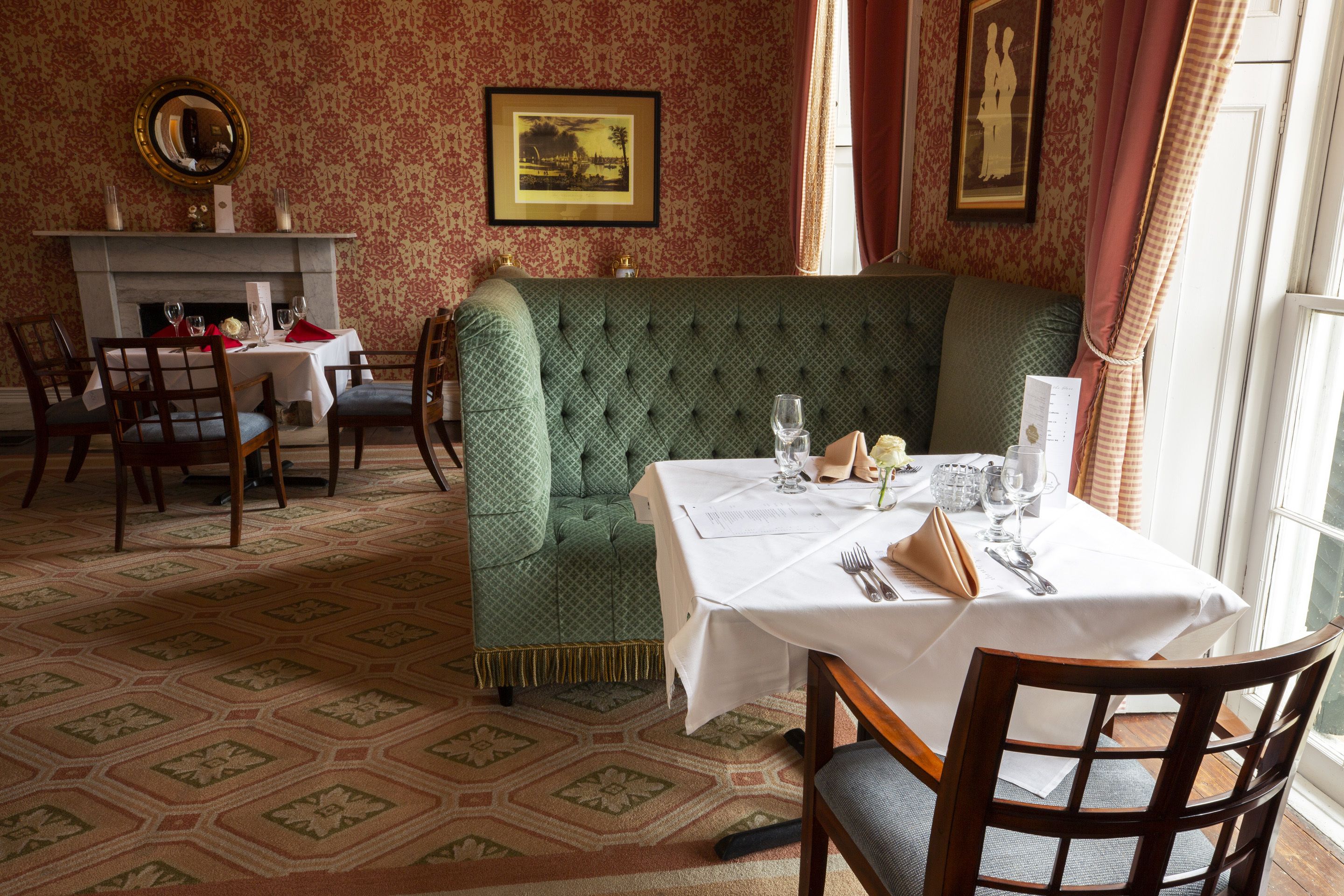 Uma área de refeições com um assento estofado verde, uma mesa branca com um cardápio e uma lareira.