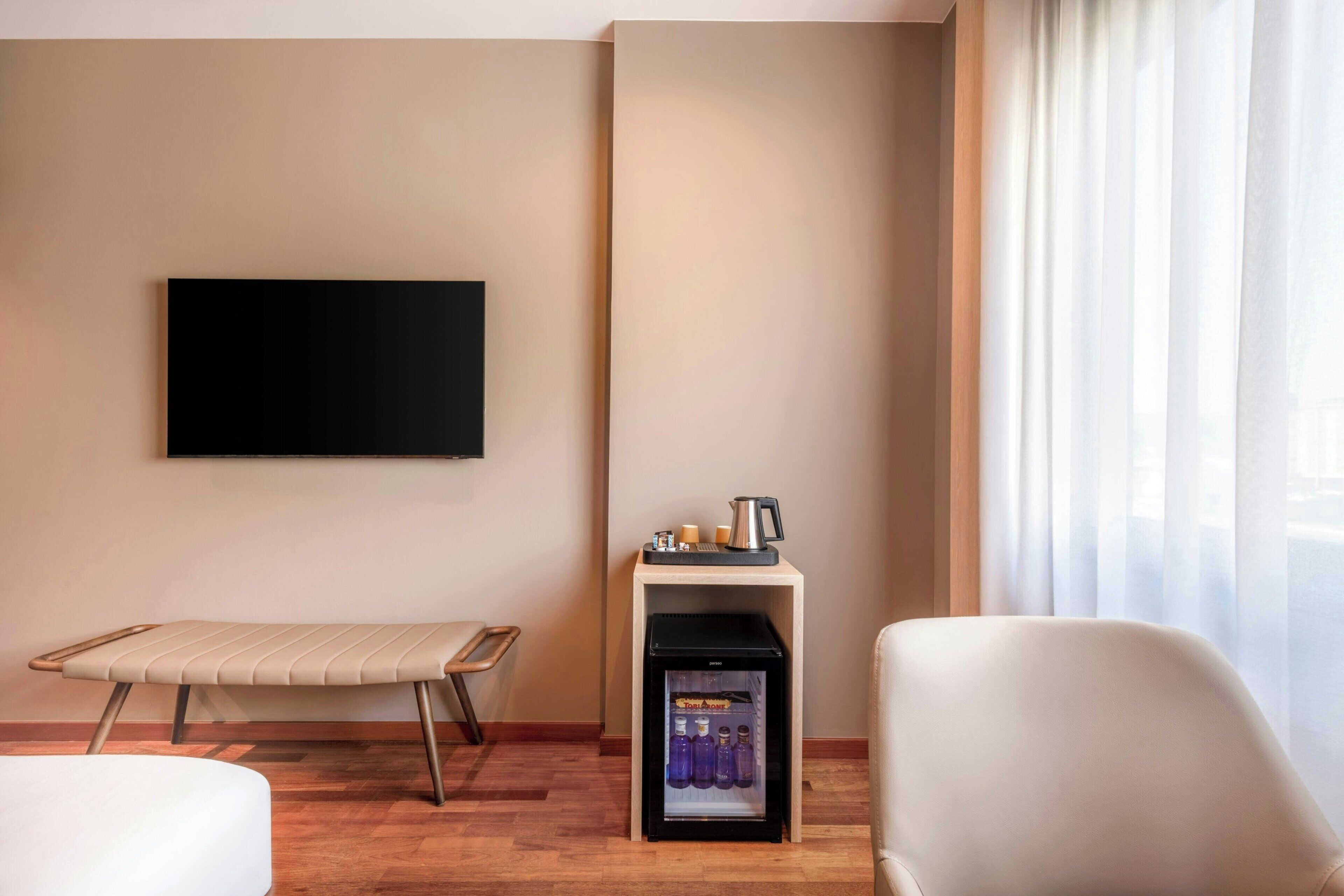 Quarto de hotel com televisão de tela plana, minibar, um banco e uma cadeira.