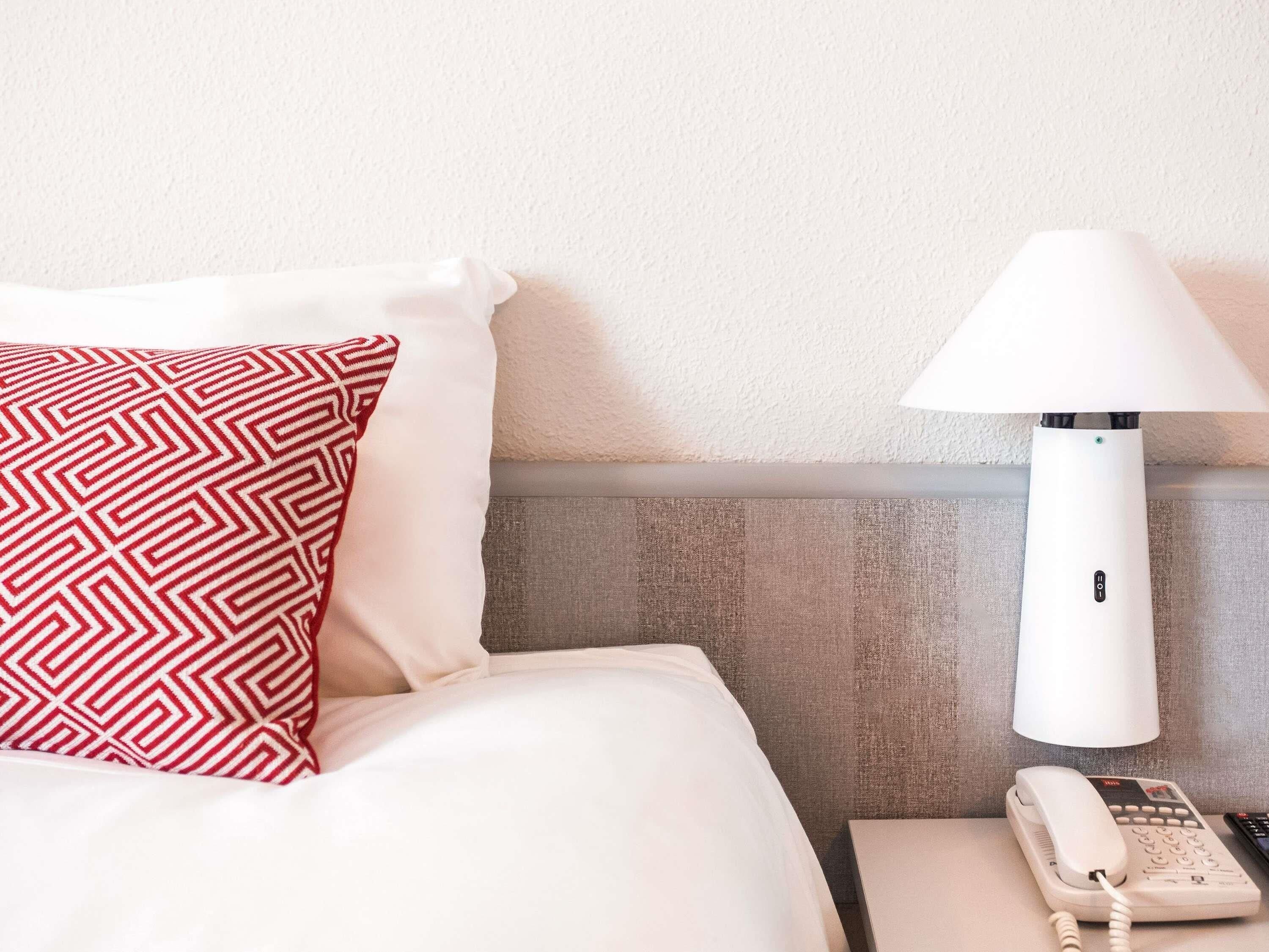 Quarto de hotel com cama, almofada estampada, abajur e telefone.