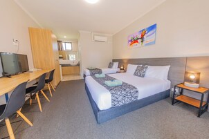 Quarto de hotel com cama, escrivaninha, cadeira, televisão e um quadro na parede.