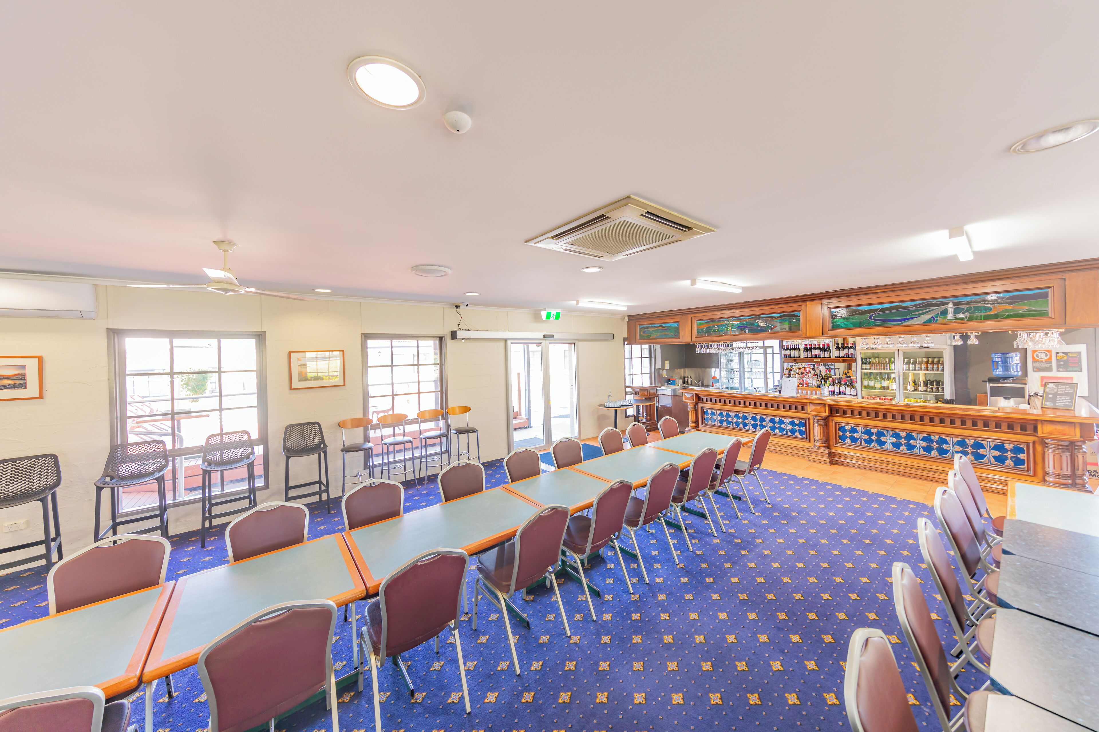 Uma sala de conferências com mesas e cadeiras, um espaço de bar com prateleiras de garrafas e um tapete estampado.