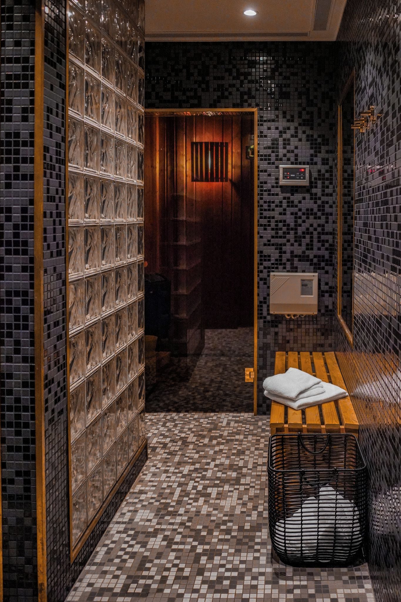Casa de banho com chão em mosaico, um banco, uma toalha e uma cesta.