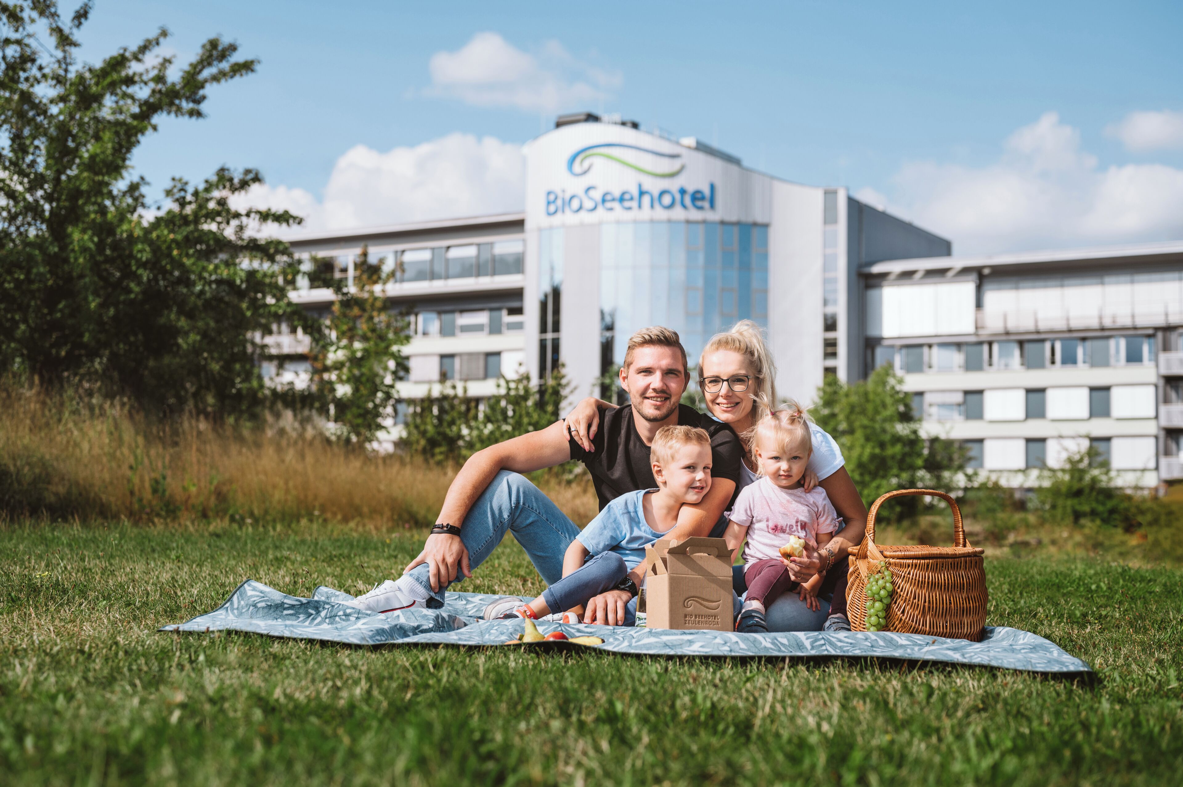 Uma família num cobertor de piquenique, com um edifício BioSeehotel ao fundo.