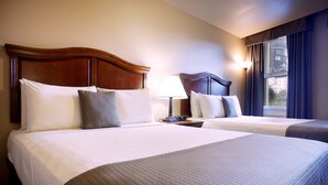 Quarto de hotel com duas camas, cada uma com cabeceira de madeira, roupa de cama branca e luminária de cabeceira.
