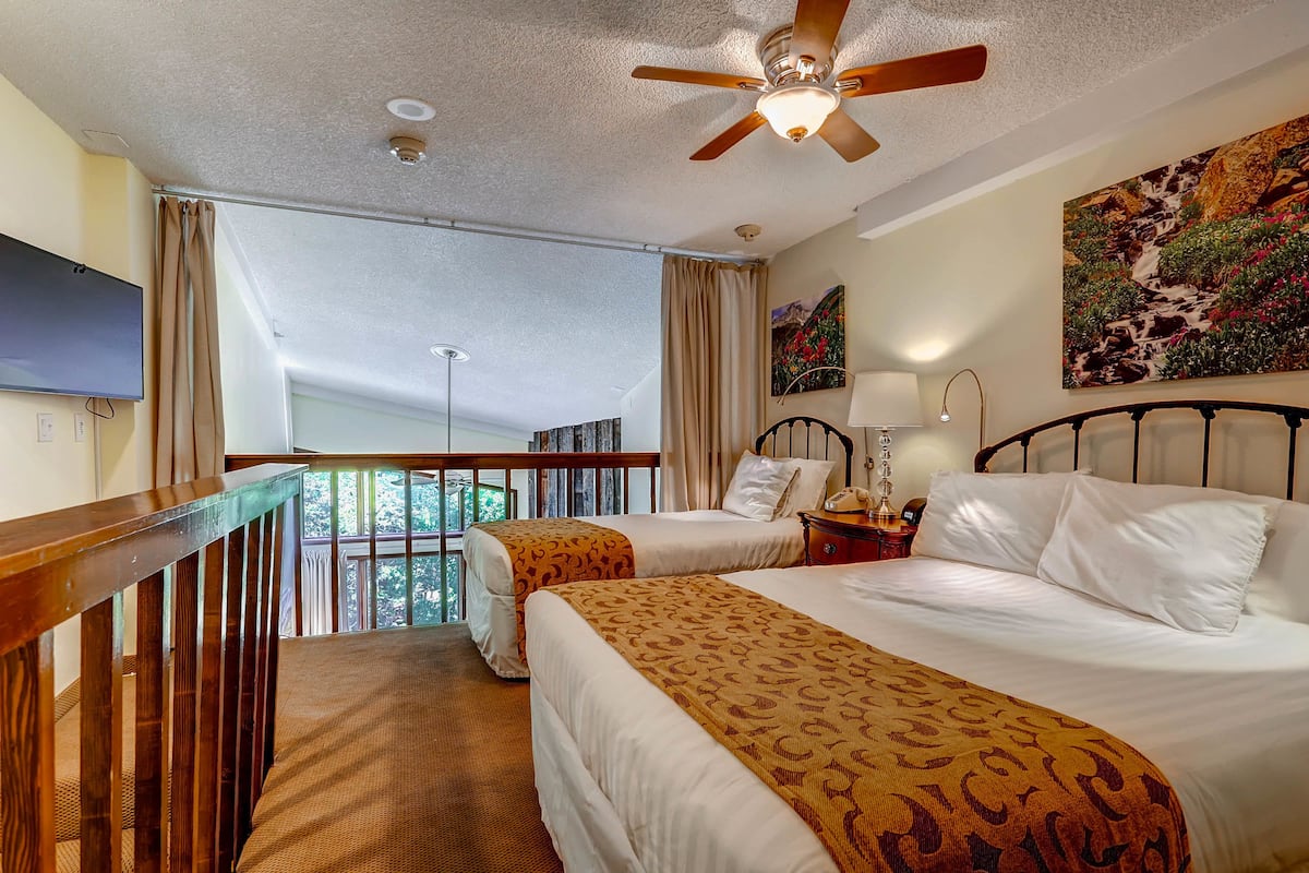 Quarto de hotel com duas camas, um ventilador de teto, um quadro e uma varanda com cortinas.