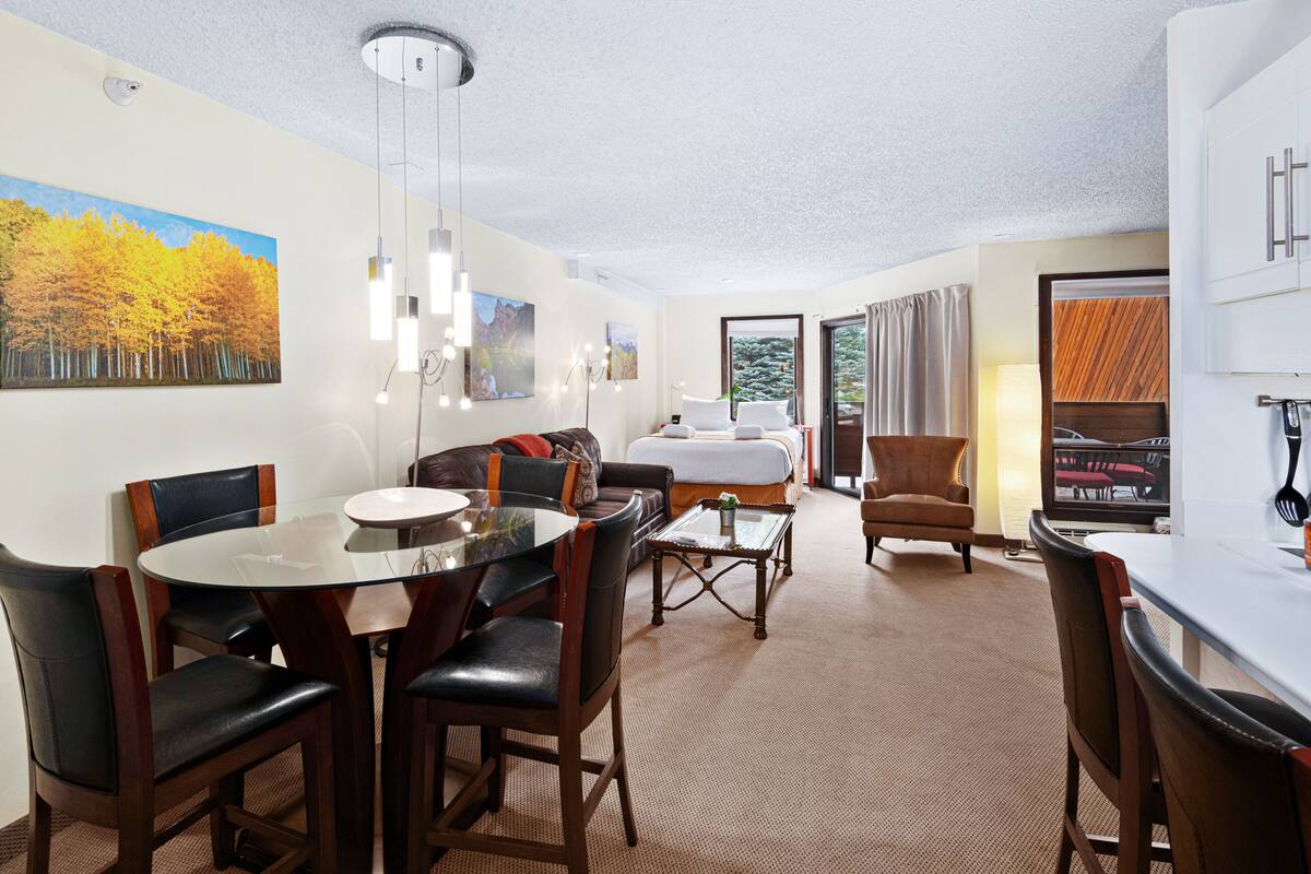 Quarto de hotel com área de jantar, sofá, cama e vista para um edifício pela janela.