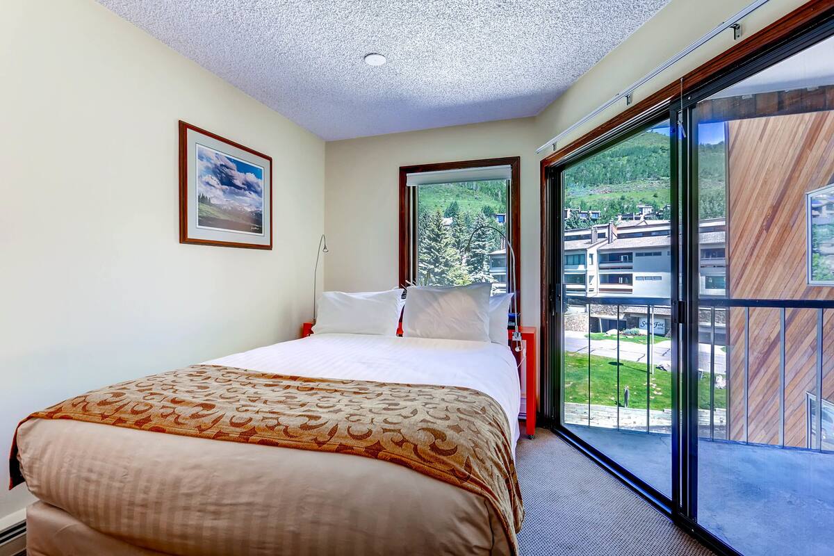 Quarto de hotel com uma cama grande, janela com vista para uma paisagem verde e um quadro na parede.