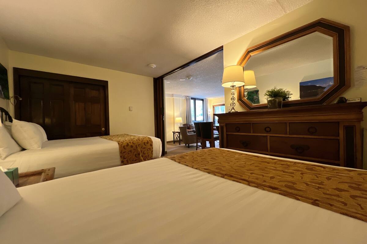 Quarto de hotel com duas camas, uma cômoda de madeira, uma escrivaninha e uma cadeira.