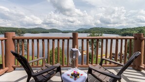 Varanda com duas cadeiras e uma mesa, com vista para um lago e montanhas ao fundo.