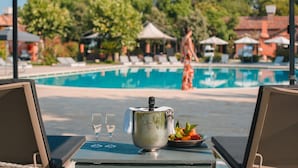 Uma mesa à beira da piscina com uma cesta de frutas, dois copos e um jarro de prata.