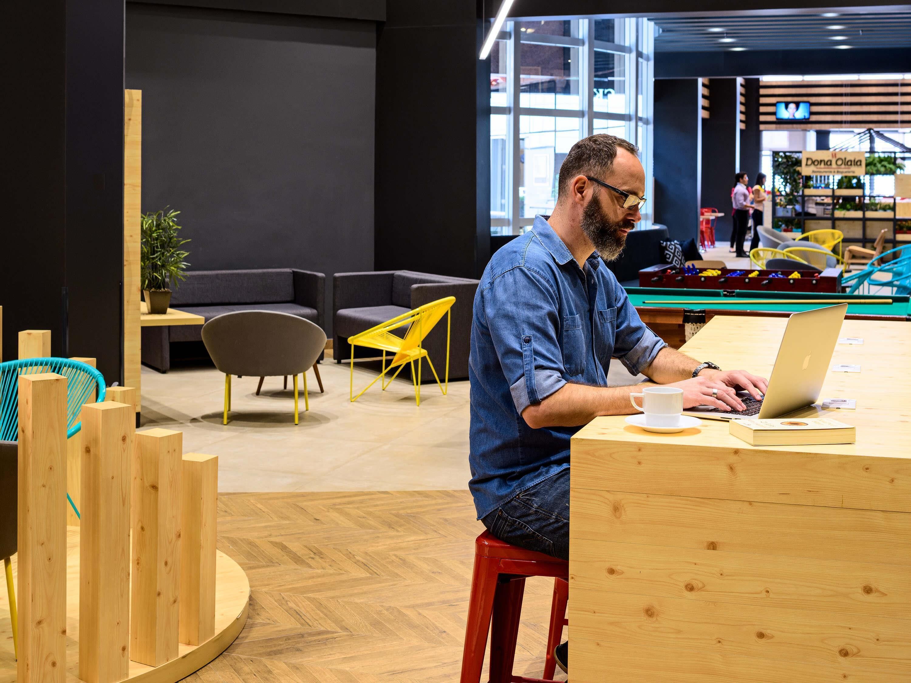 Um homem trabalha num laptop num espaço de escritório moderno com móveis de madeira e mesa de bilhar.